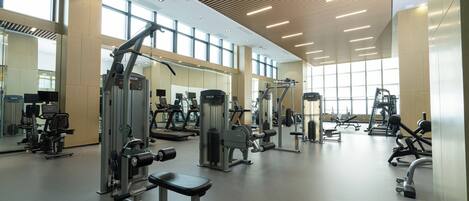 Uma academia espaçosa com diversos equipamentos de exercício, grandes janelas e um teto alto com ripas de madeira.