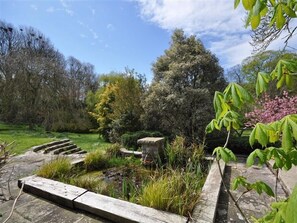 Um jardim com degraus de pedra que levam a um lago, rodeado por diversas árvores e arbustos.