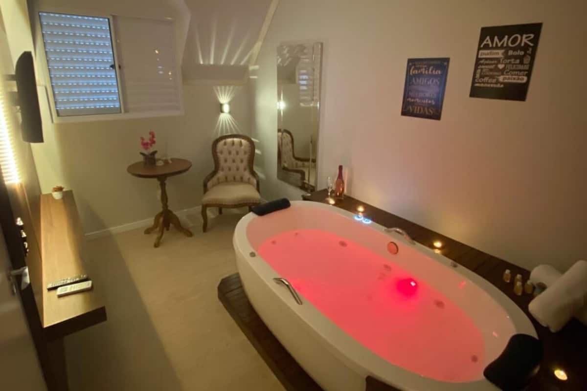 Um quarto de spa com uma banheira de hidromassagem, uma mesa pequena com um vaso, uma cadeira e um espelho.
