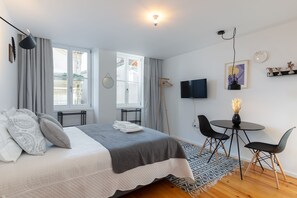 Quarto moderno com cama grande, televisão, mesa de jantar pequena e vista para o exterior.