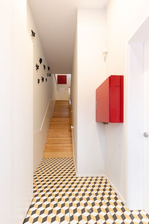 Um corredor estreito com piso xadrez, escada de madeira e um armário vermelho.