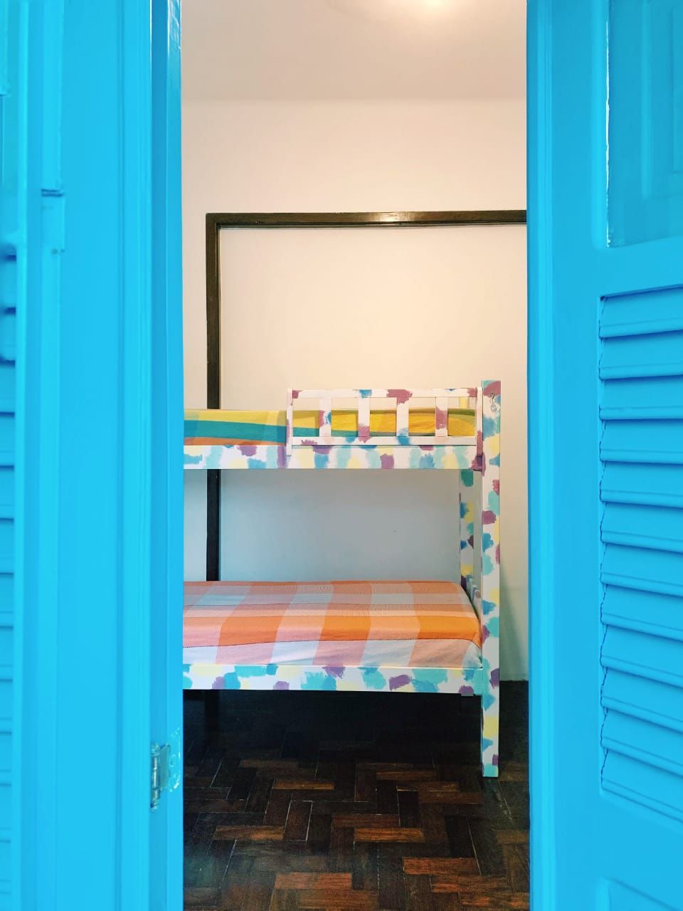Uma cama beliche com colchão colorido e parede branca ao fundo.