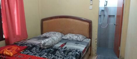 Quarto com cama, chuveiro e ar-condicionado fixado na parede.
