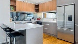Uma cozinha moderna com ilha central, eletrodomésticos de aço inoxidável, armários de madeira e um espaço com banquetas.