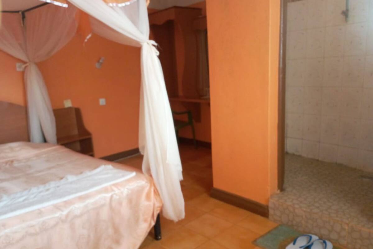 Quarto com cama, mesa de cabeceira, cadeira e zona de duche.