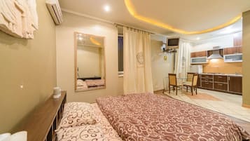 Quarto com uma cama grande, escrivaninha e cozinha compacta.