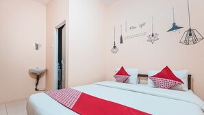 Cama bem arrumada com colcha vermelha e branca, duas almofadas com padrão repetido e três luminárias pendentes de designs variados.