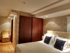 Quarto de hotel com uma cama, uma cadeira, um guarda-roupa e um papel de parede estampado.
