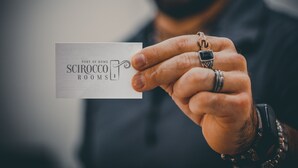 Uma mão segurando um cartão de visita com o texto 'Port of Rome Scirocco Rooms'.