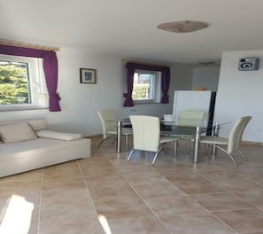 Uma sala de estar moderna com mesa de jantar de vidro, sofá branco e cortinas roxas.