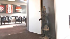 Um corredor com uma porta branca, uma estátua e uma sala de jantar com mesas e cadeiras.