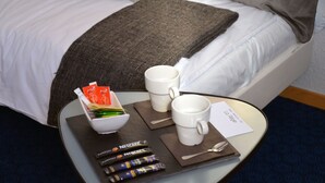 Uma bandeja de café da manhã bem organizada sobre uma mesa pequena, com duas canecas brancas, um copo de suco de laranja e uma embalagem de cápsulas de café Nespresso.