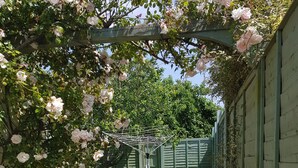 Um jardim com uma escultura de coruja branca, uma pérgola coberta de rosas e uma mesa com cadeiras.