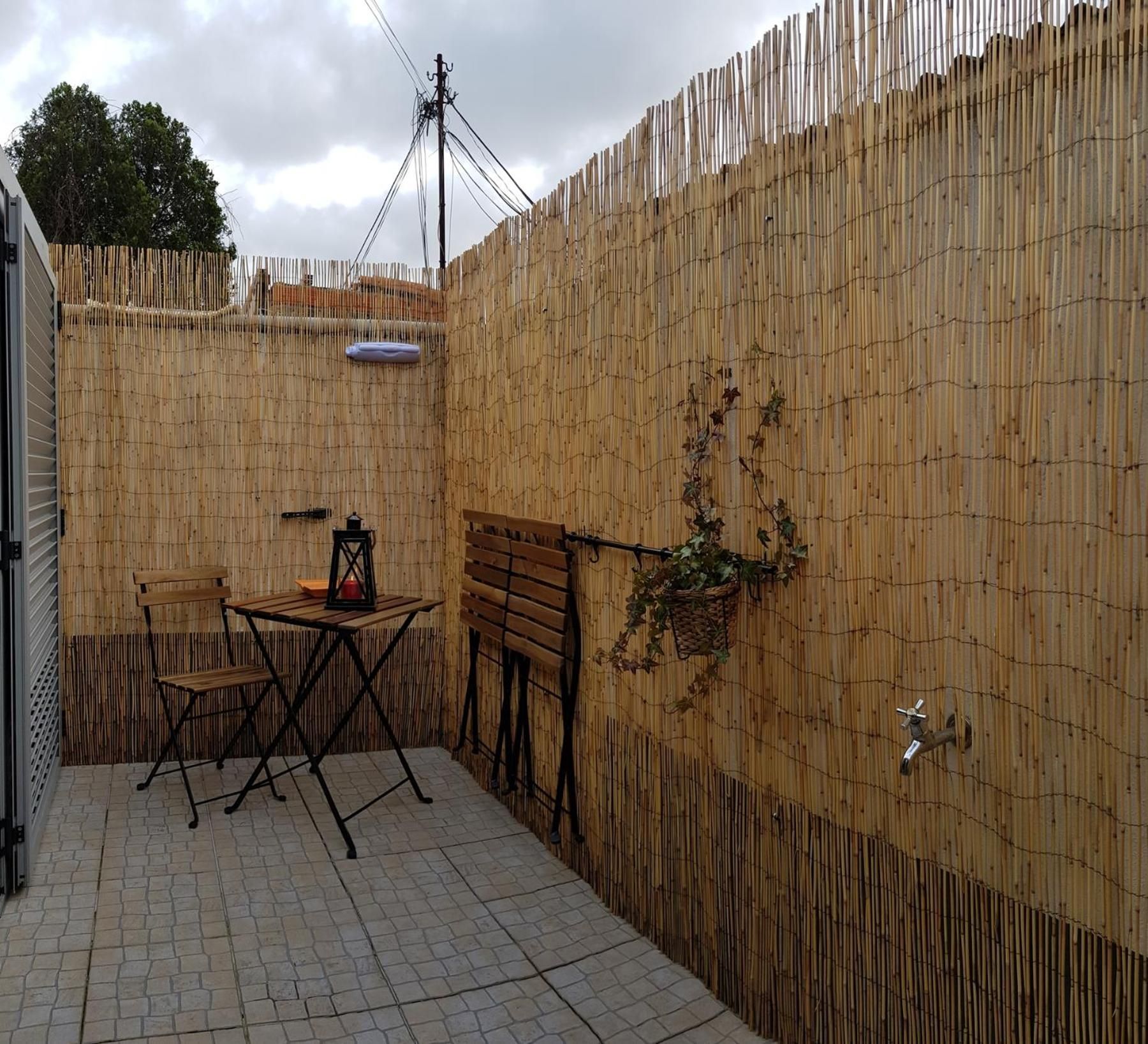 Área de pátio com cerca de bambu, uma mesa com cadeiras e uma planta pendente.