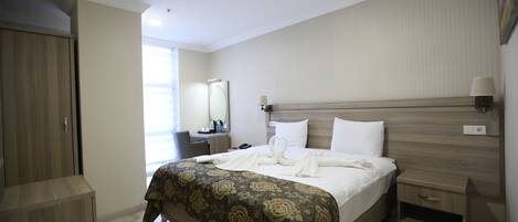 Quarto de hotel com uma cama grande, um guarda-roupa de madeira, uma mesa de cabeceira com abajur e um espelho na parede.