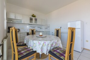 Cozinha compacta com armários brancos, uma ilha central com toalha de mesa florida e uma geladeira.