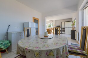Uma área de refeições com uma mesa redonda coberta por uma toalha florida, uma pequena vela branca e uma geladeira azul.
