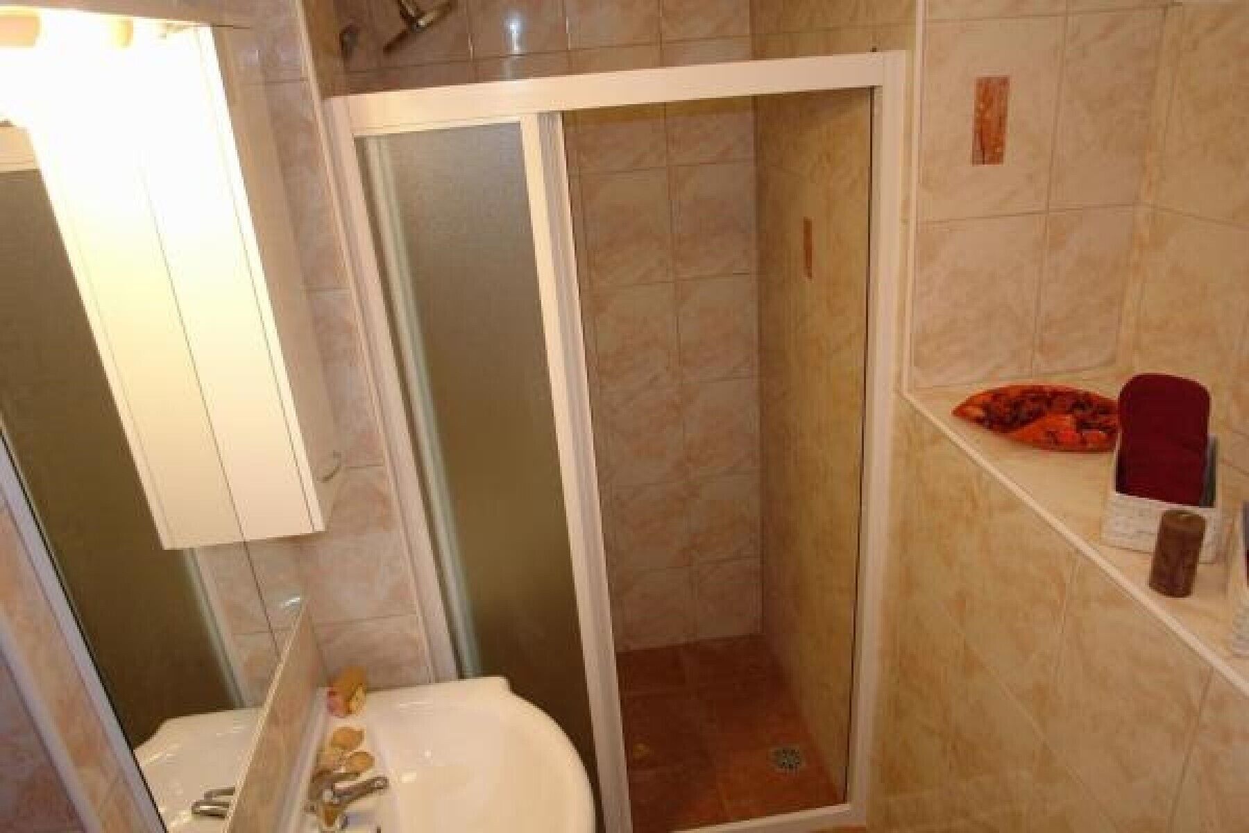 Casa de banho com chuveiro, pia e prateleira com artigos de higiene.