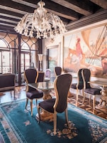 Um quarto com um candelabro, uma pintura grande de uma paisagem urbana e uma mesa com cadeiras.