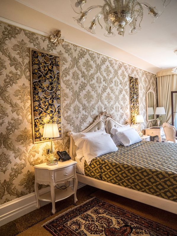 Quarto de hotel clássico com uma cama grande, uma mesa de cabeceira, uma escrivaninha e um candelabro.