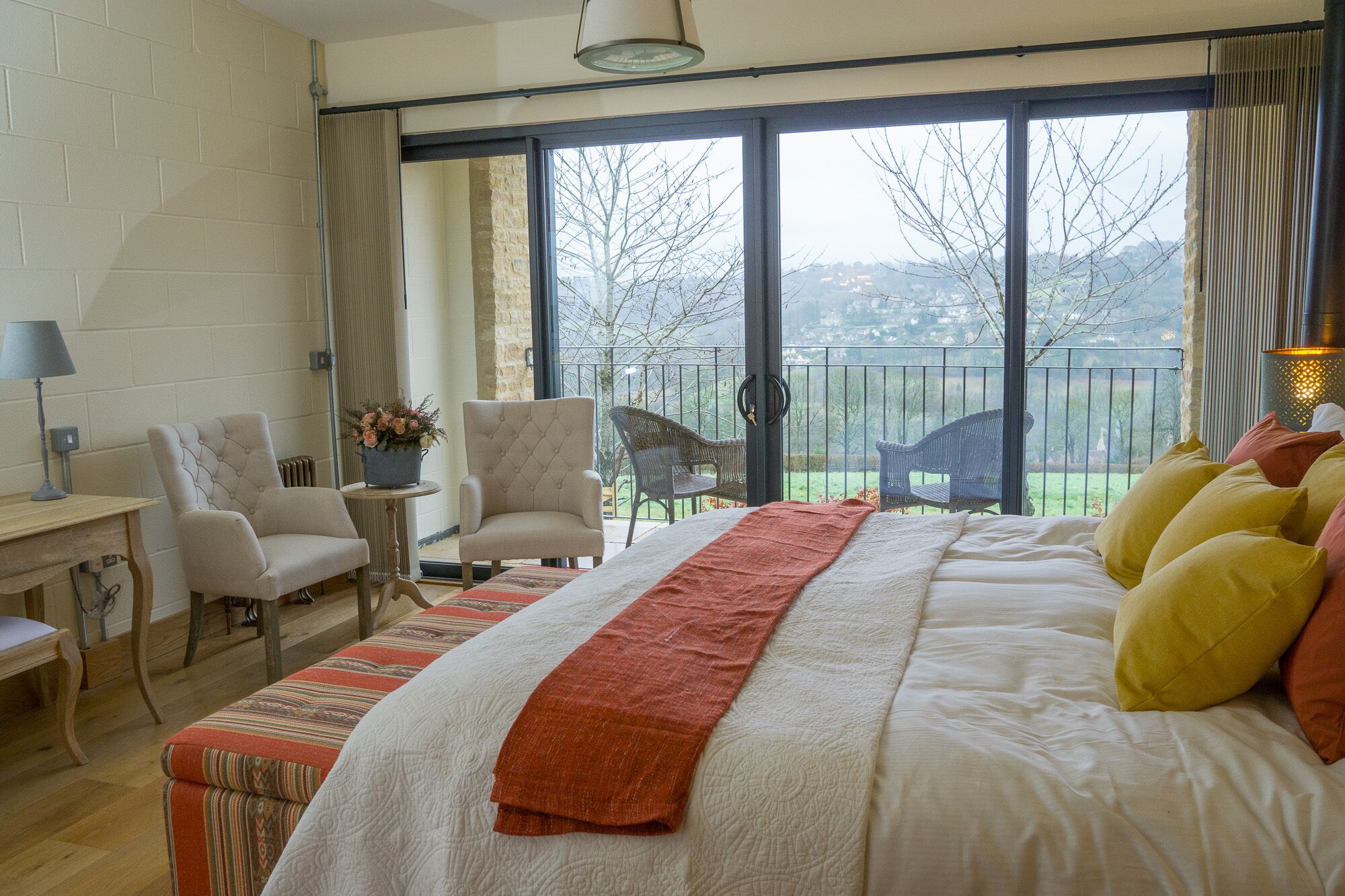 Quarto com cama grande, escrivaninha, cadeira e varanda com cadeiras.