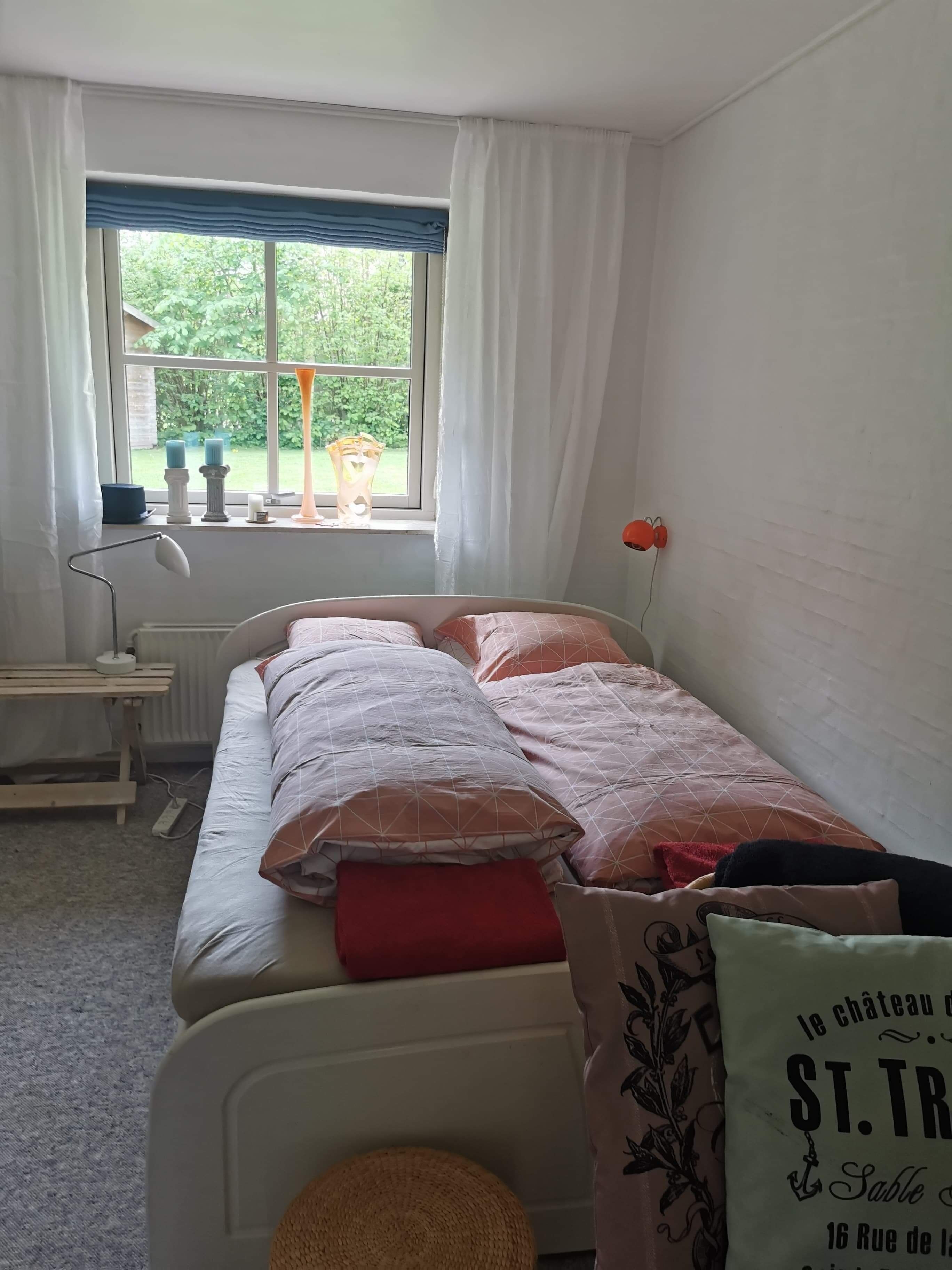 Um quarto com uma cama, uma mesa de cabeceira, um abajur e uma janela com cortinas.