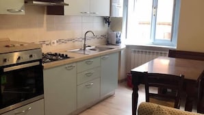 Cozinha compacta com fogão a gás, pia e armários. Há uma mesa de jantar com cadeiras e um sofá na sala.