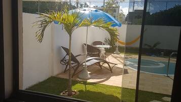 Um pátio com uma mesa e cadeiras, uma pequena palmeira e um guarda-sol azul.