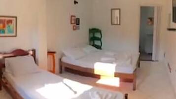 Quarto com duas camas, uma cadeira verde e porta para outro cômodo.