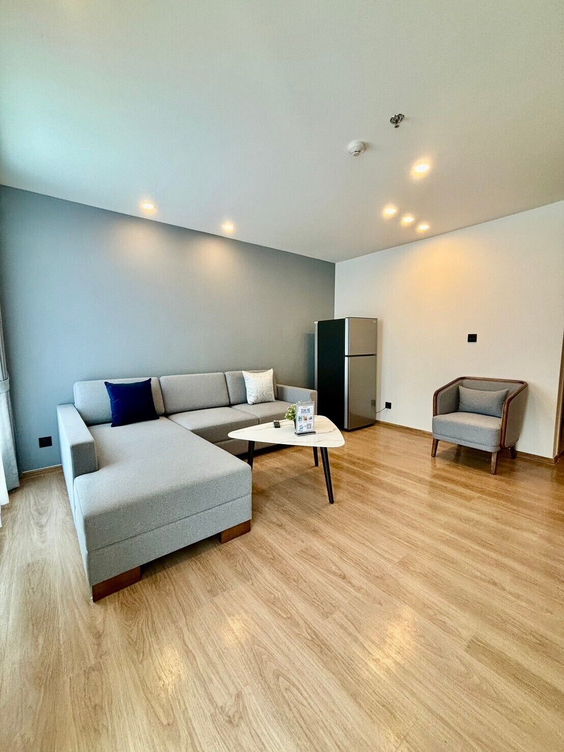Uma sala de estar moderna com um sofá seccional cinza, uma mesinha de centro redonda e uma poltrona cinza.