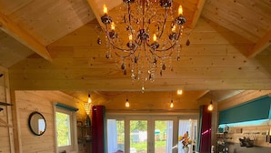 Interior acolhedor de uma cabana de toras, com uma cama grande, um candelabro, uma área de jantar e uma cozinha.