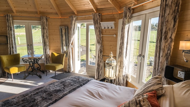 Quarto de madeira com uma cama, uma mesa e cadeiras, e vista para o exterior.