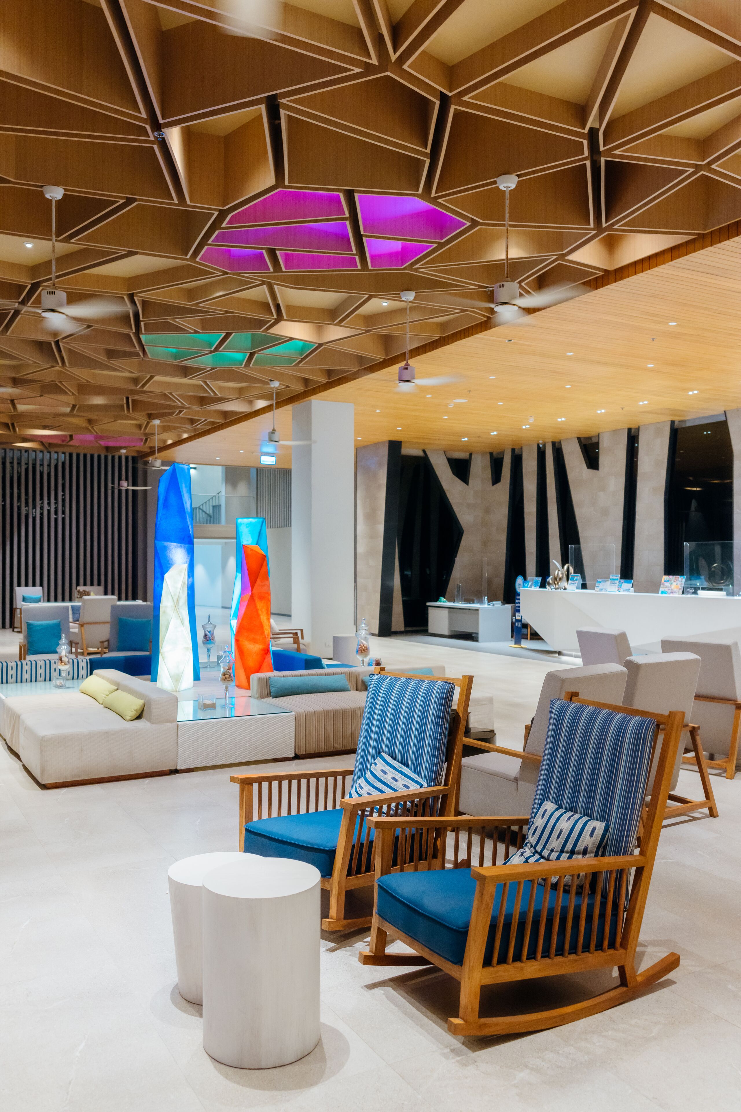 Um lobby moderno com design geométrico no teto, áreas de estar e balcão de recepção.
