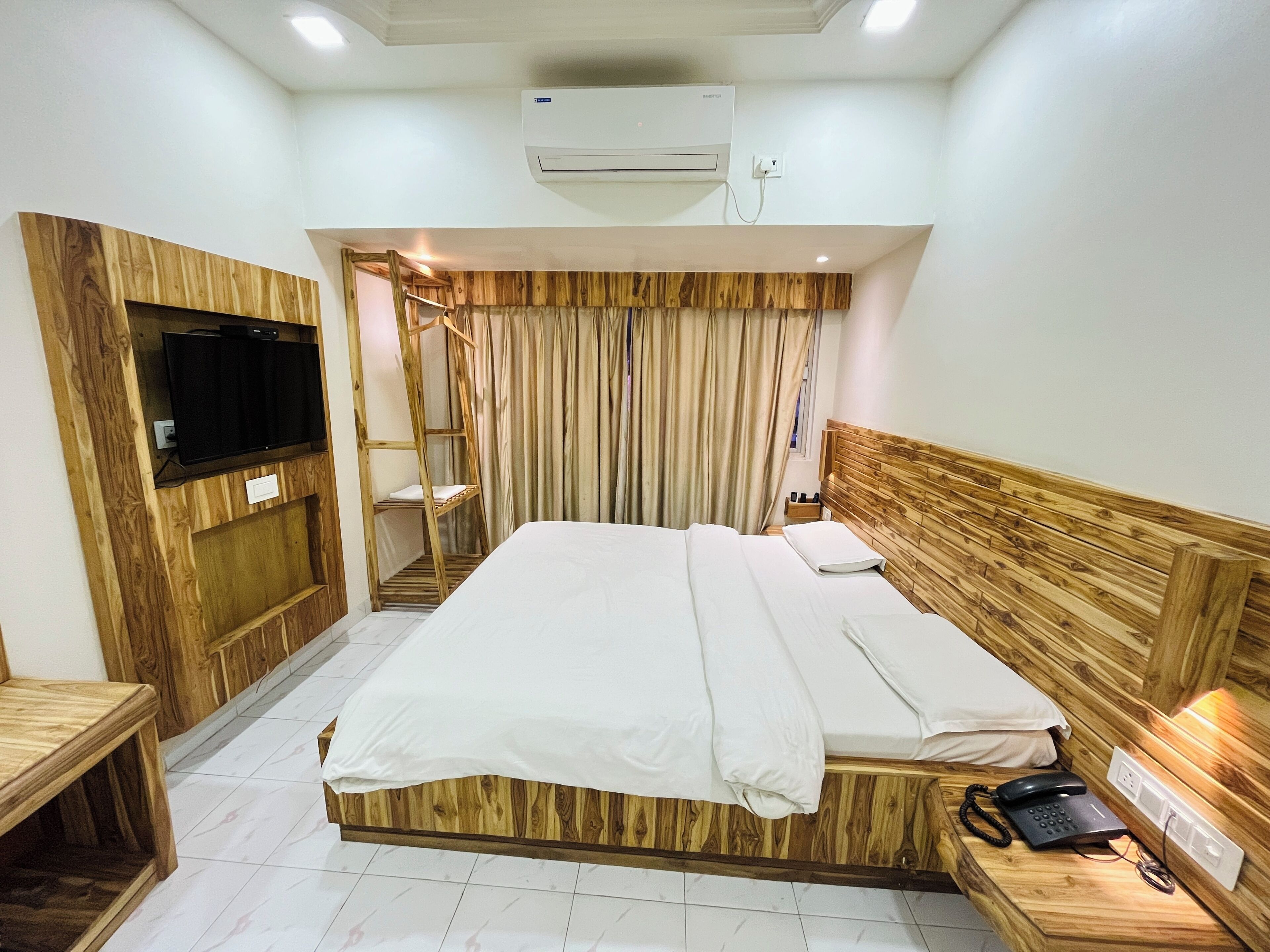 Quarto de hotel com cama de madeira, televisão na parede, telefone ao lado da cama e ar condicionado.