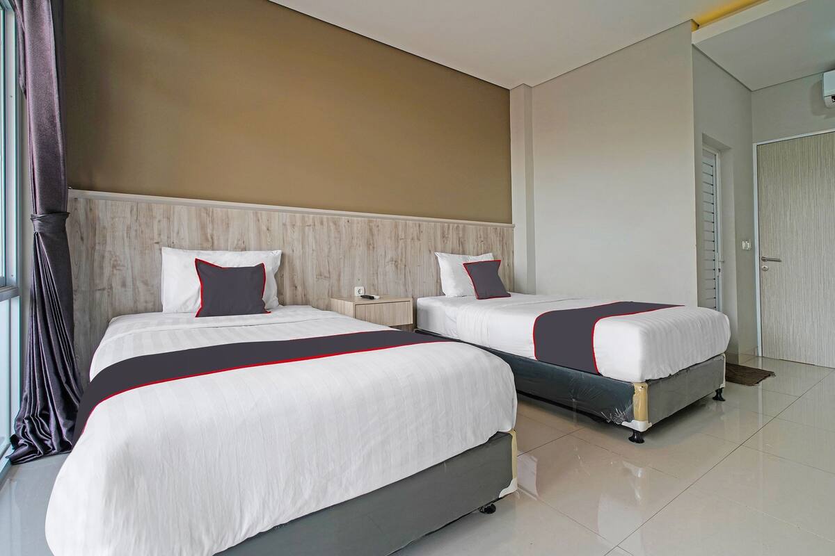 Quarto de hotel com duas camas, cabeceira de madeira, mesa de cabeceira e uma porta.