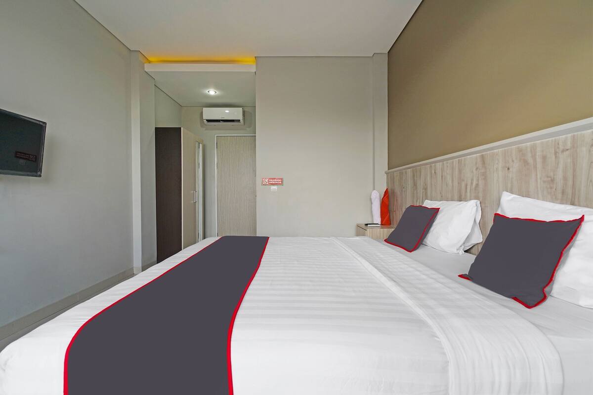 Quarto de hotel com uma cama grande, mesa de cabeceira e televisão na parede.