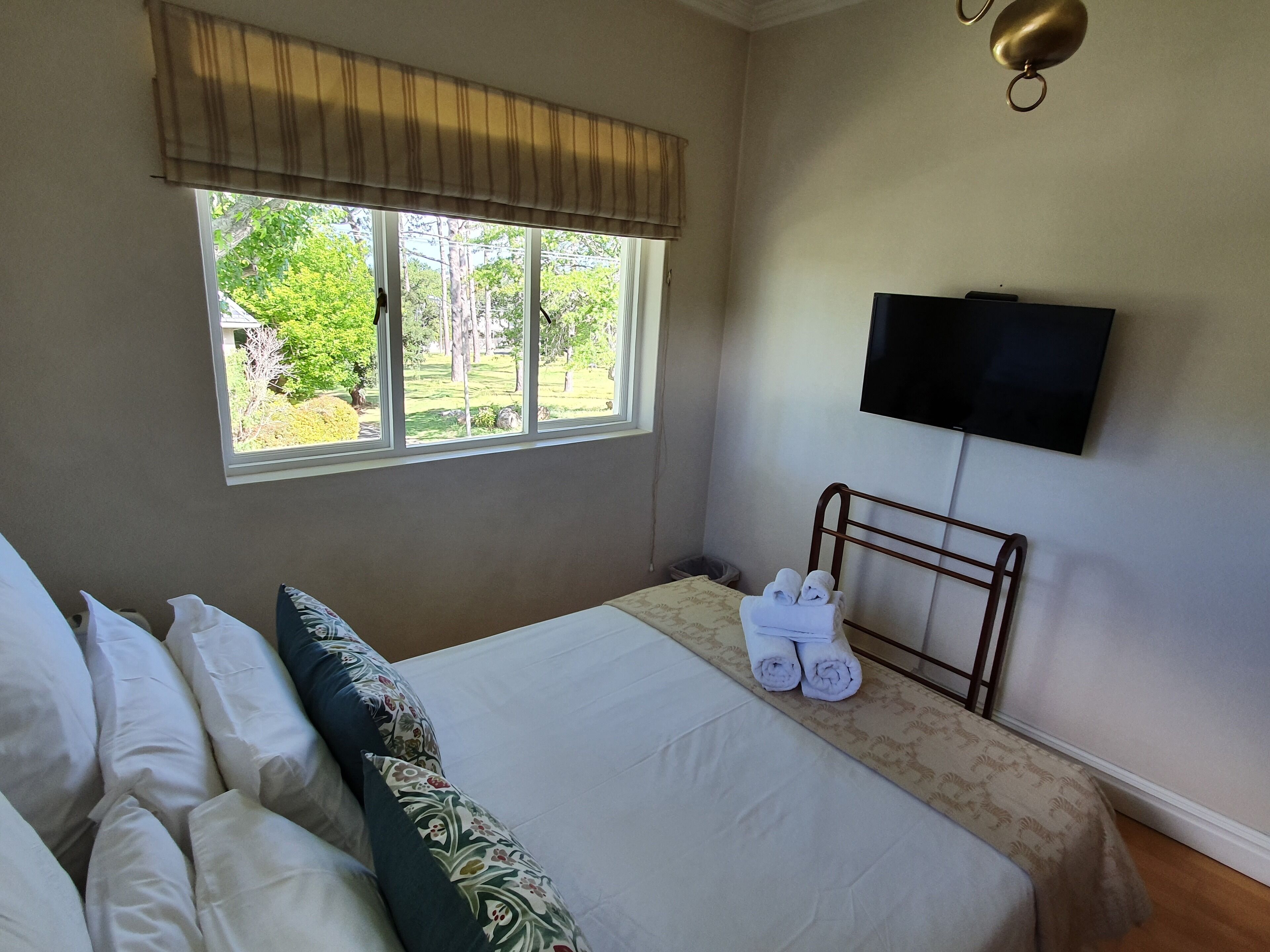 Quarto de hotel com uma cama, uma televisão presa à parede e uma janela com vista para o verde lá fora.