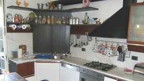 Uma cozinha compacta com fogão, forno e pia. Há prateleiras sobre o balcão com diversos utensílios de cozinha.