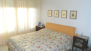 Um quarto com uma cama, uma mesa de cabeceira e uma parede com três quadros.