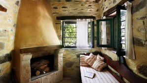 Um quarto rústico de pedra com lareira, uma cama com roupa de cama listrada e uma janela com persianas verdes.