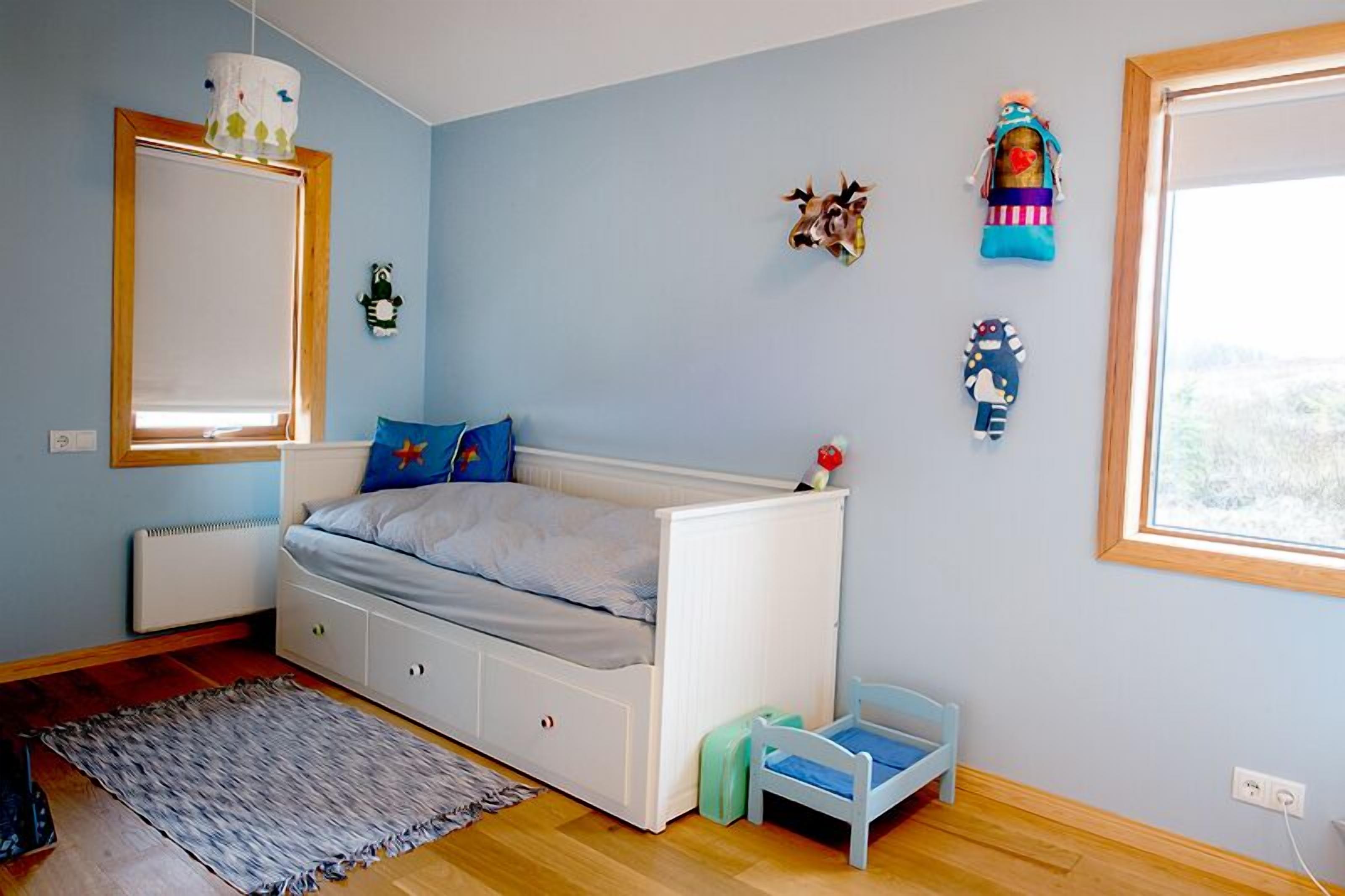 Quarto de criança com cama branca, cadeira azul pequena, janela e decorações nas paredes incluindo cabeças de animais.