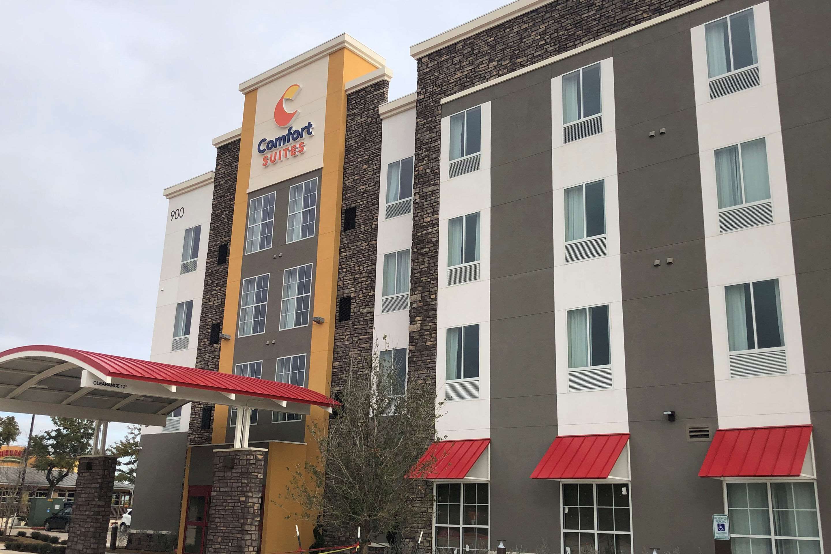 Um hotel com vários andares e placa 'Comfort Suites', com fachada que combina pedra e design moderno, e toldos vermelhos no andar térreo.