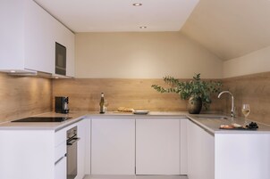 Uma cozinha moderna com armários brancos, painel de madeira, forno embutido, pia e uma planta em vaso.