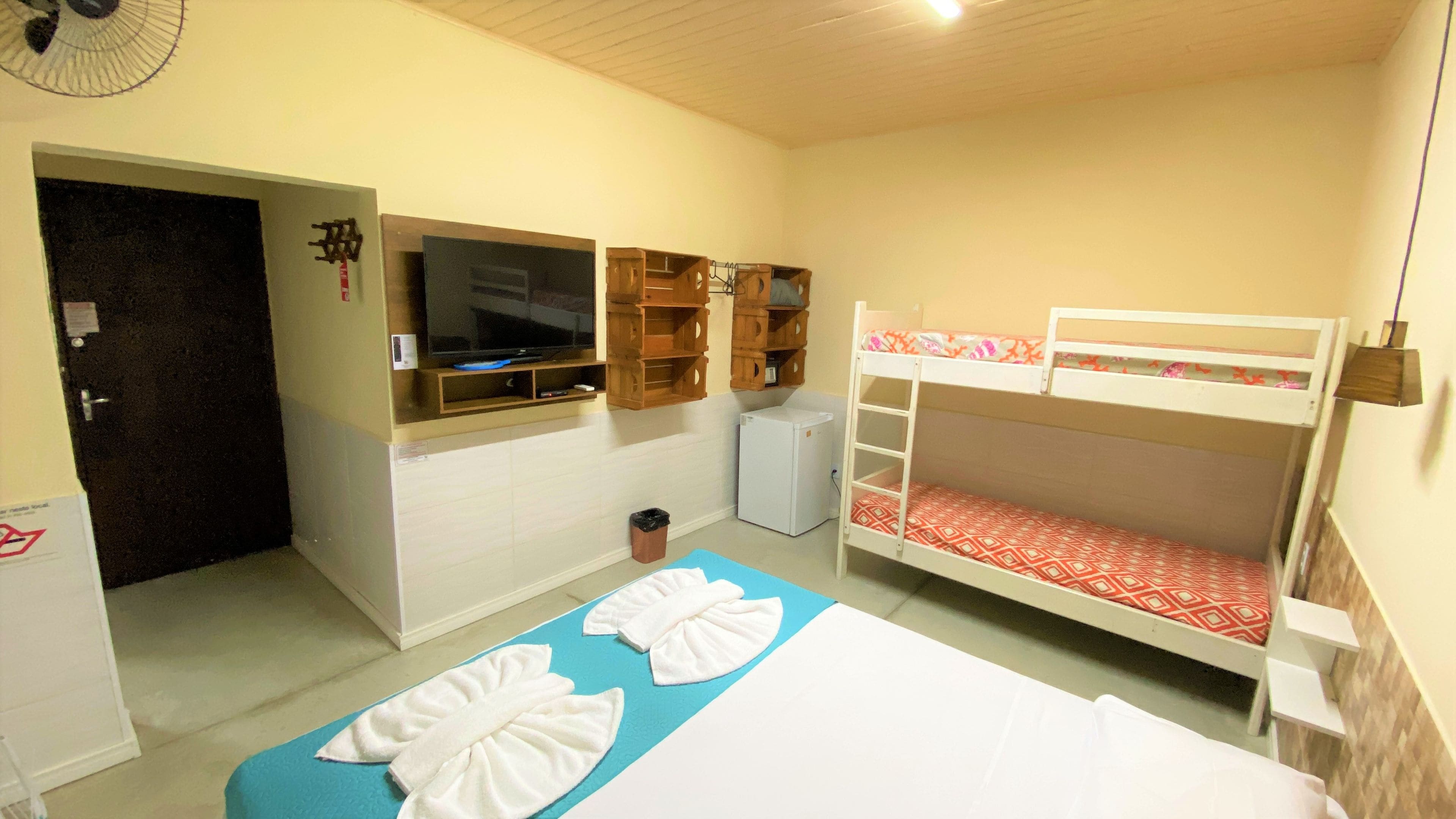 Quarto com beliches, televisão, mini-geladeira e ventilador.