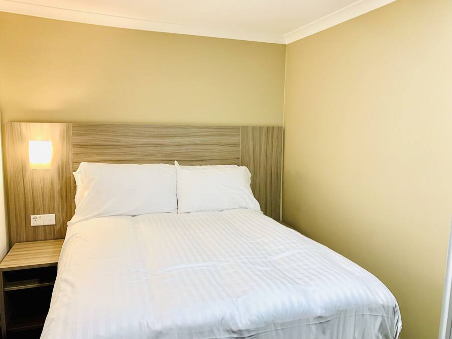 Cama bem arrumada com lençóis brancos num quarto com paredes bege e cabeceira de madeira.