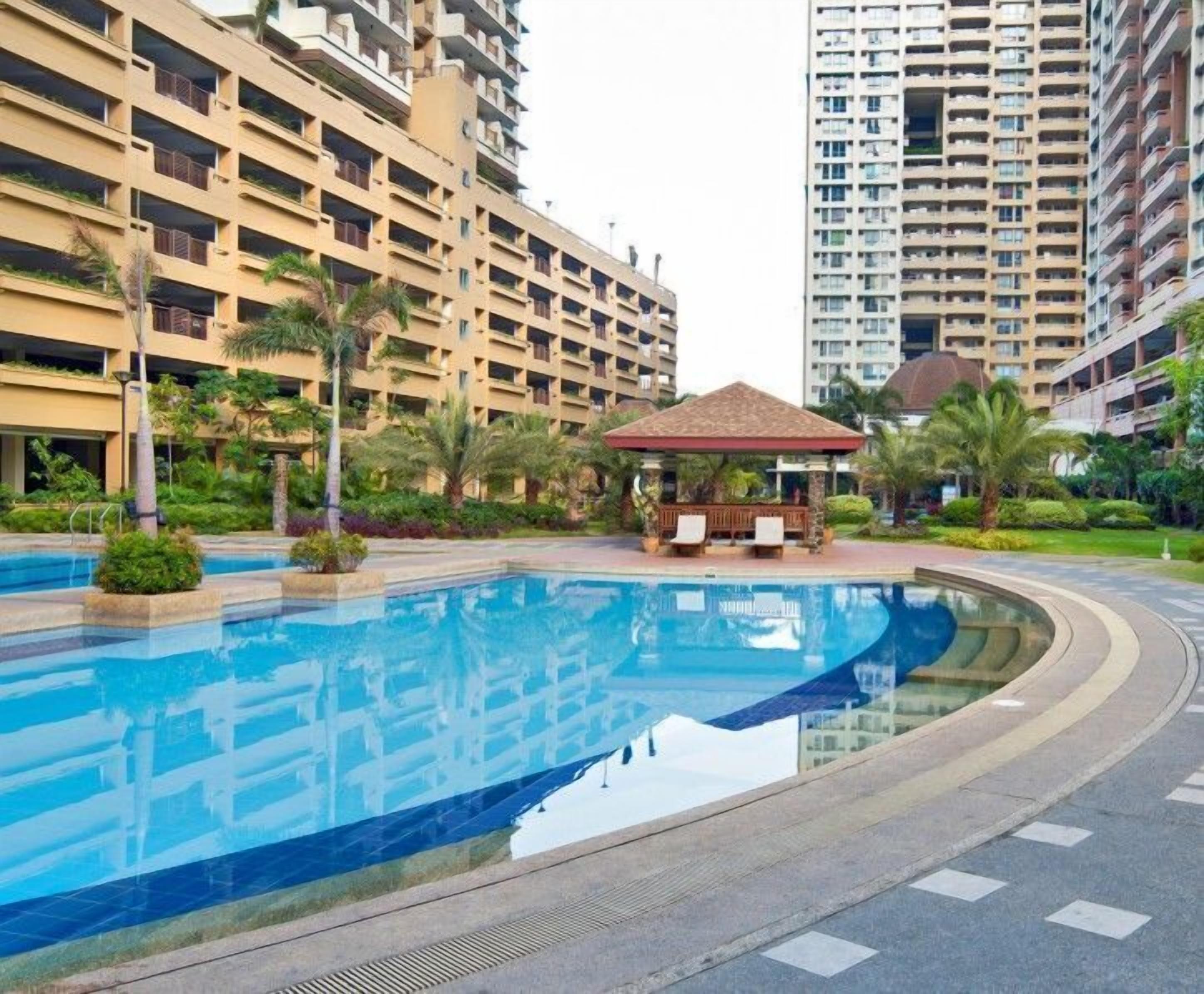Piscina rodeada por vegetação exuberante e edifícios residenciais altos.