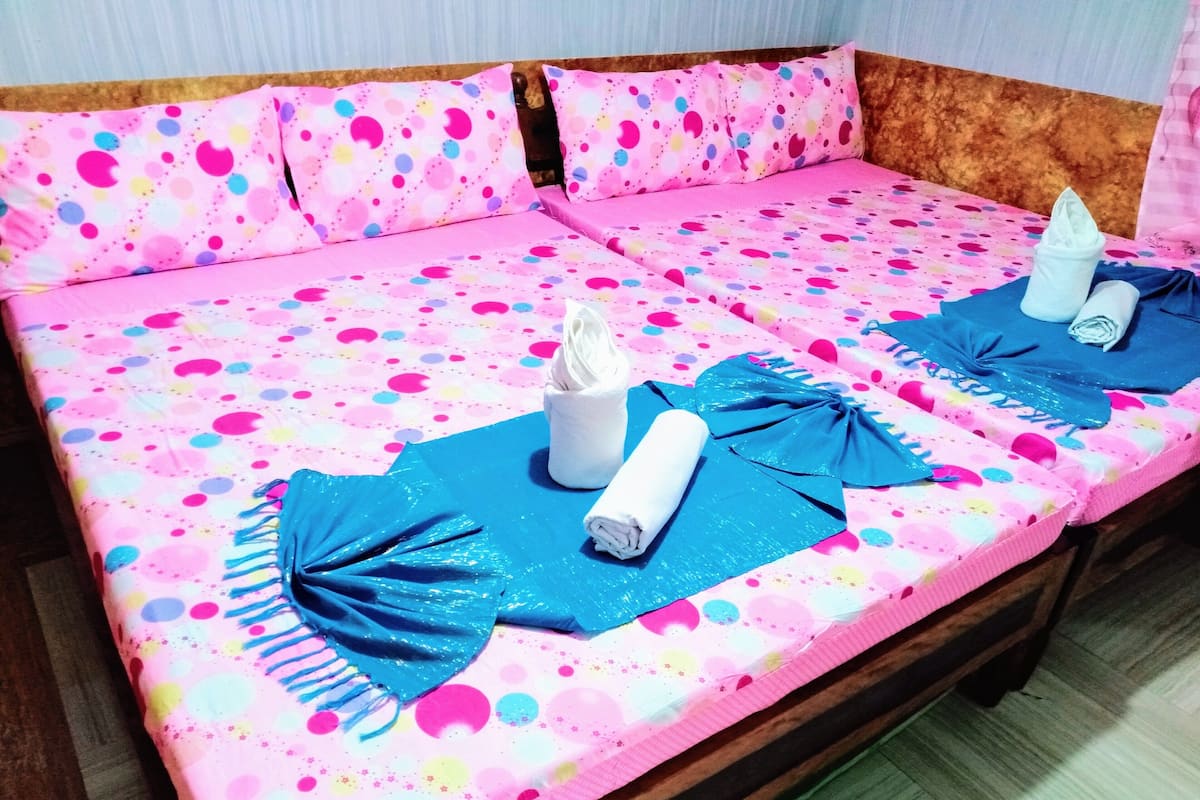 Cama com colcha rosa e azul com bolinhas, dois travesseiros e toalhas dobradas com cuidado.