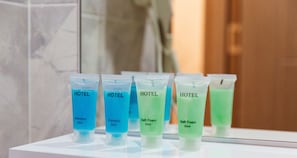 Exposição de produtos de higiene pessoal de hotel, incluindo shampoo e espuma de banho em embalagens transparentes.