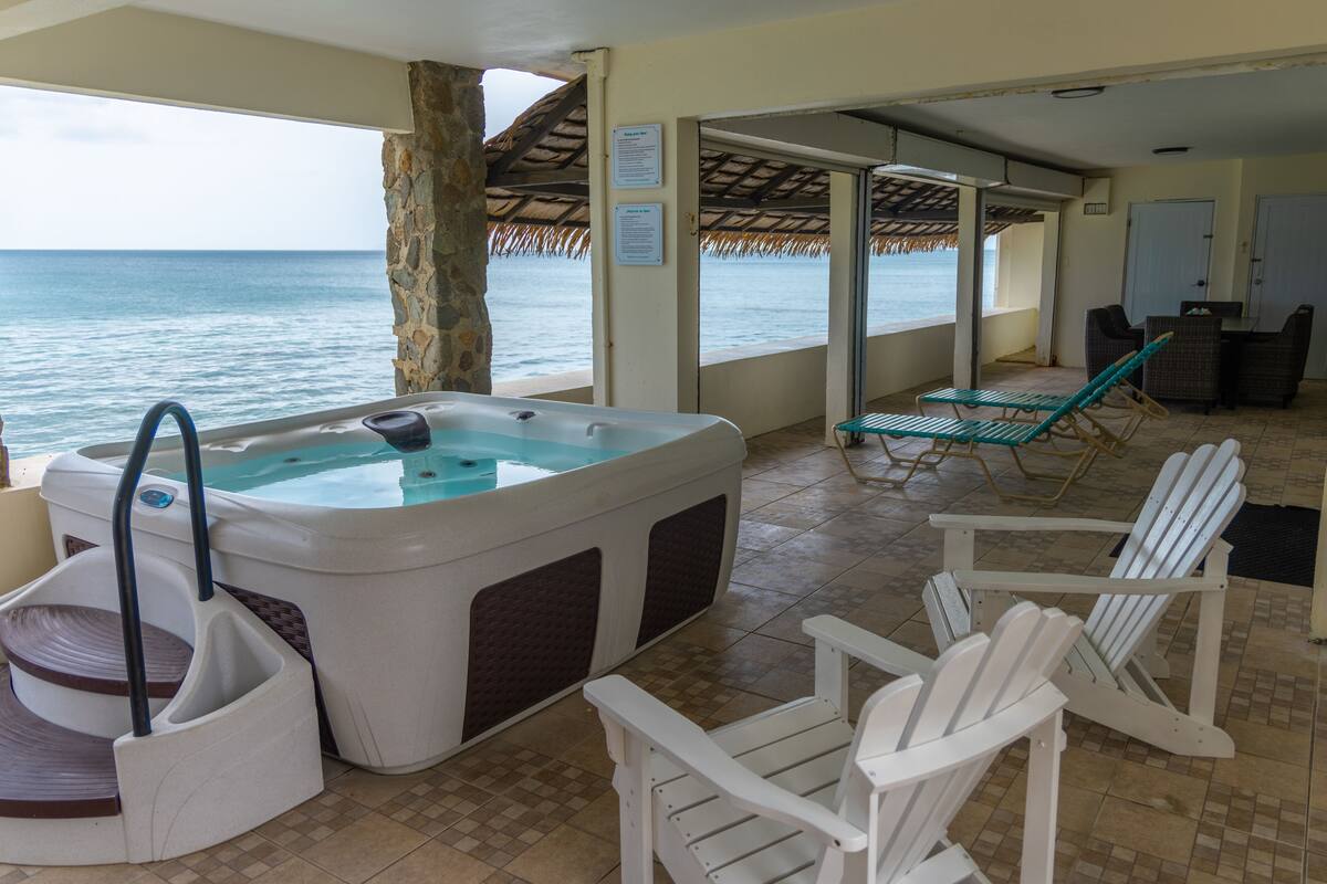 Uma banheira de hidromassagem e espreguiçadeiras perto de uma janela com vista para o mar.