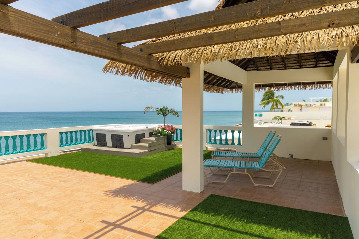 Um alpendre coberto com vista para o oceano, uma piscina e uma área de estar com cadeiras.